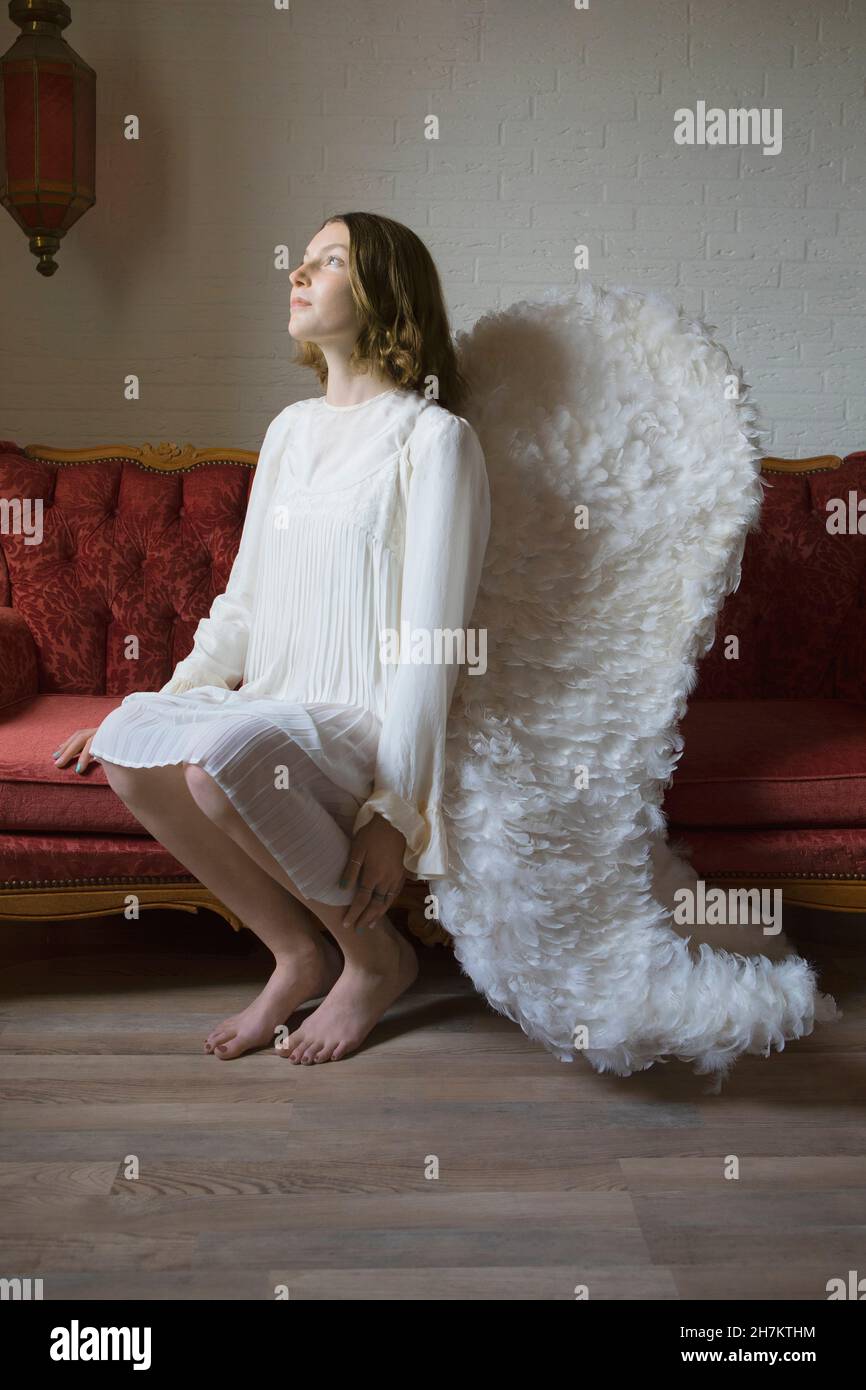 Angel wearing white wings contemplating on sofa Stock Photo - Alamy