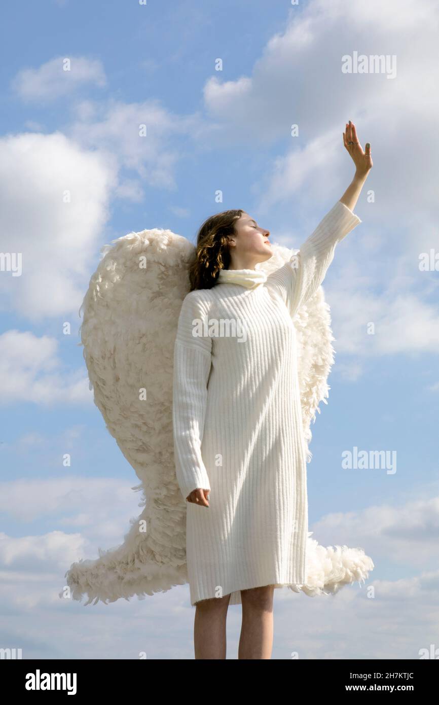 Angel wearing white wings with hand raised Stock Photo - Alamy