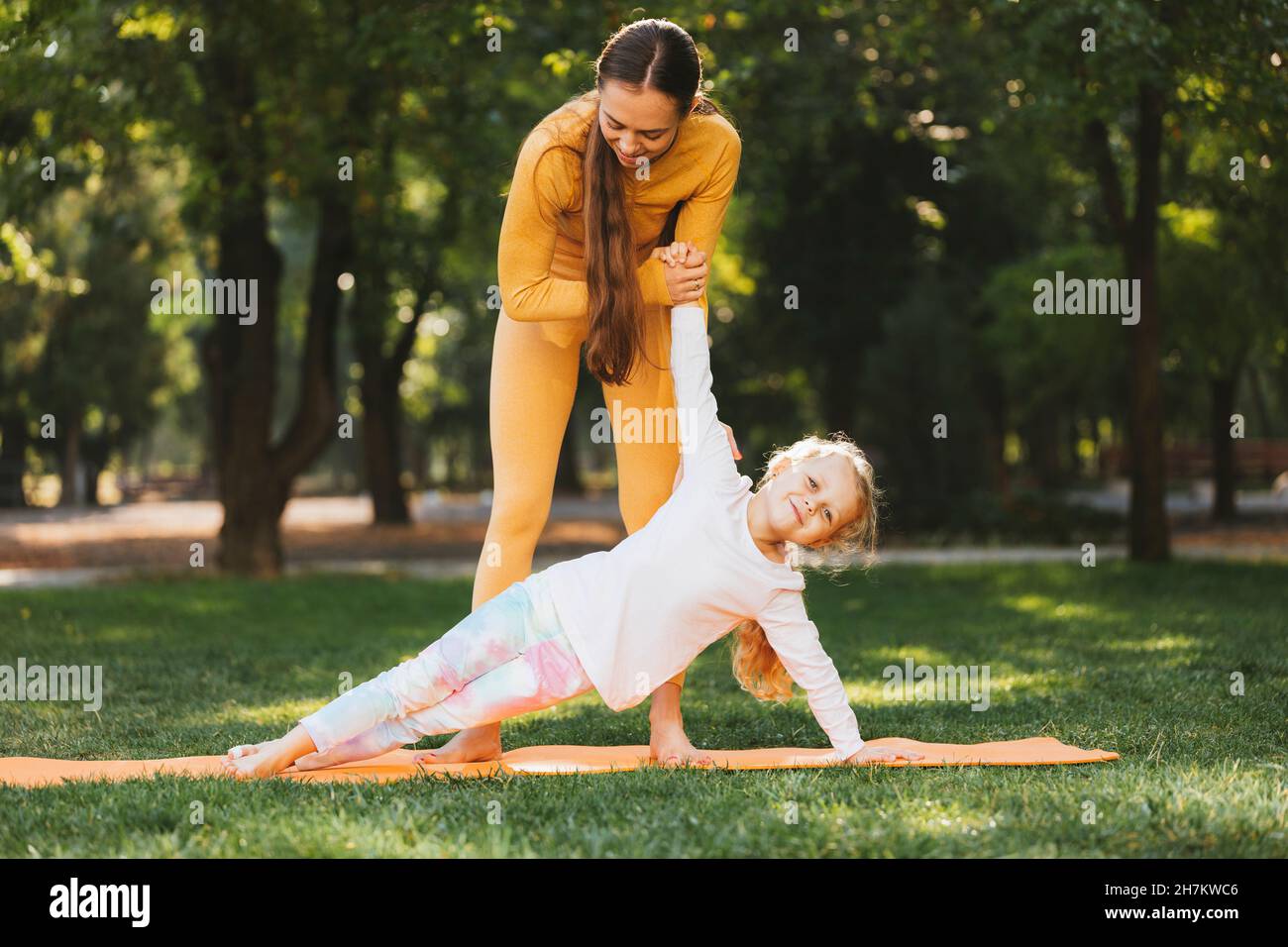 Mother helping daughter practicing yoga in park Stock Photo - Alamy