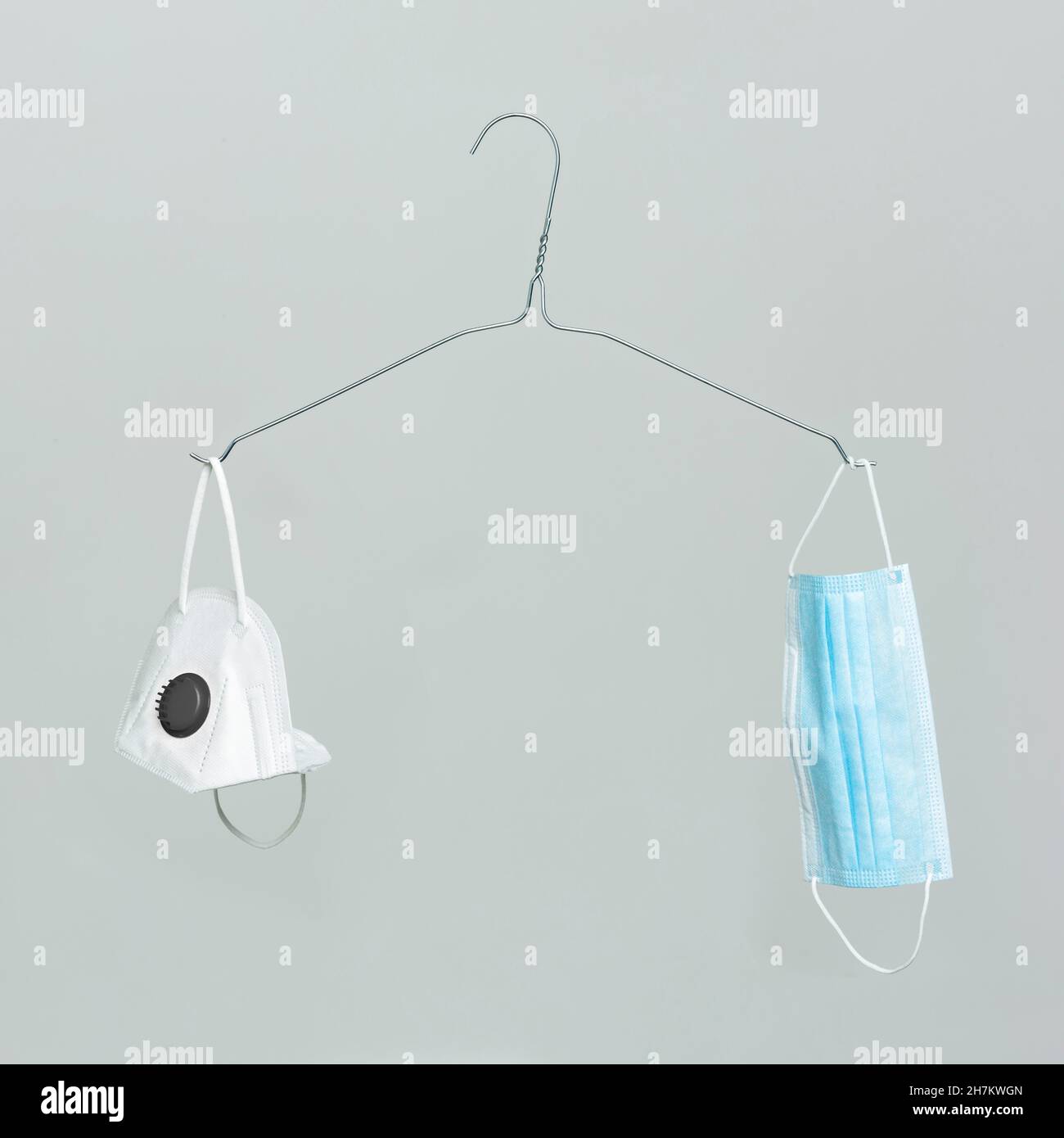 Two protective face masks hanging on coathanger against gray background ...