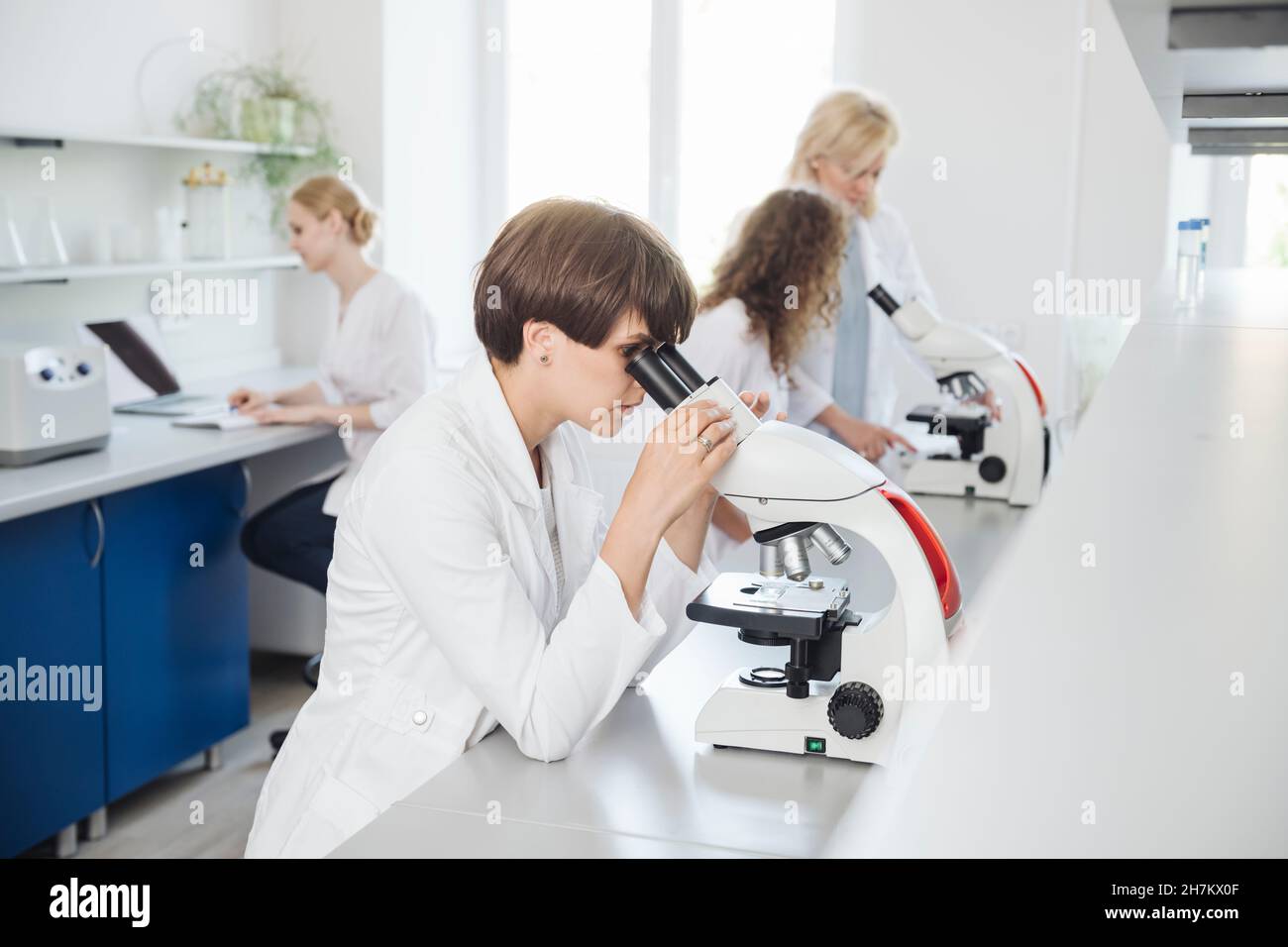 Researcher using microscope with colleagues working in background Stock ...