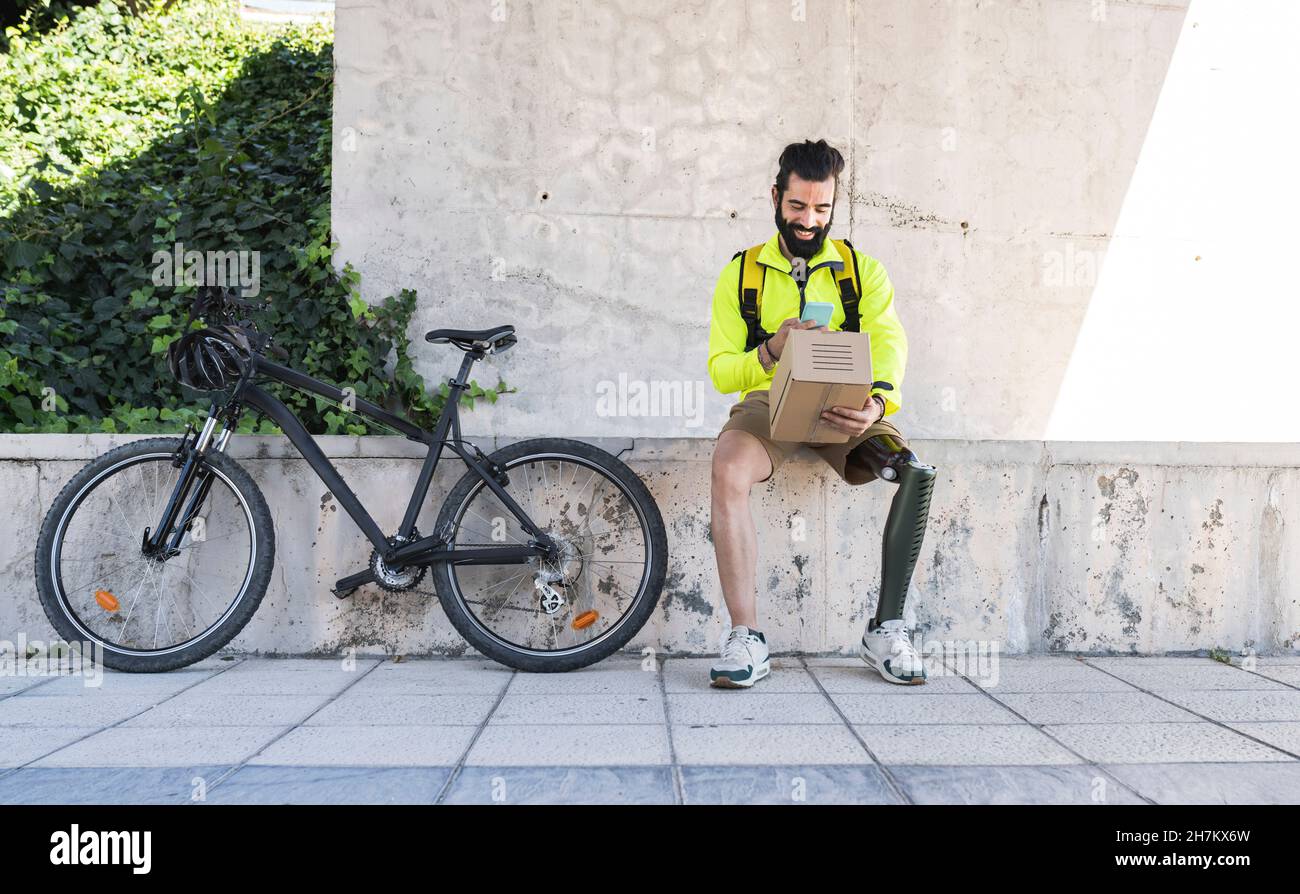 Smiling disabled delivery man scanning box with mobile phone by bicycle ...