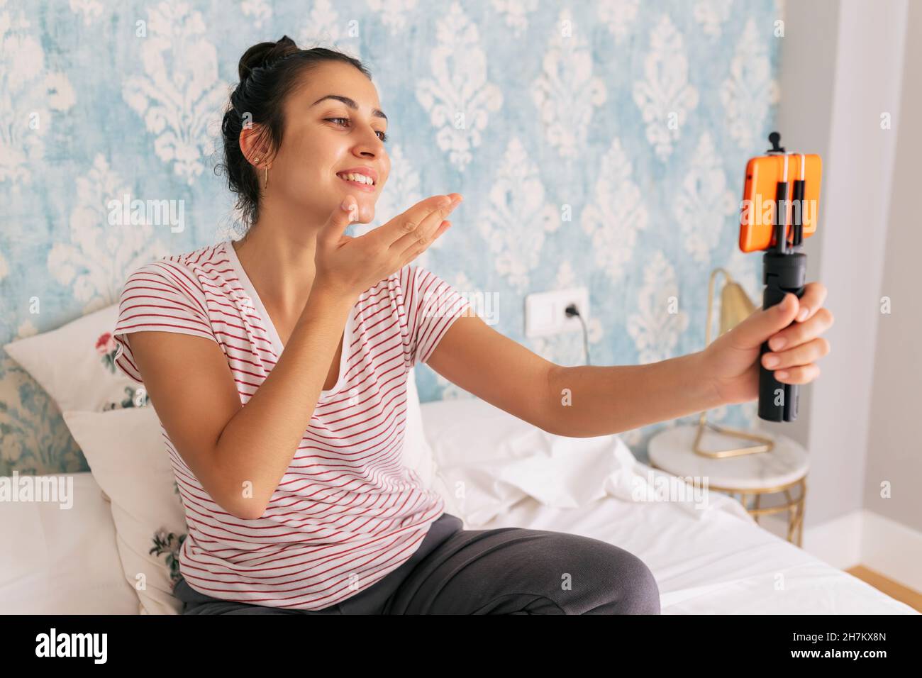 Smiling female influencer vlogging through mobile phone in bedroom ...