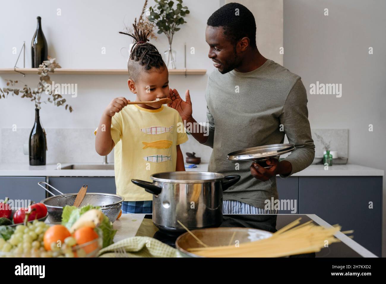 Young man talking with son smelling spaghetti in kitchen Stock Photo ...
