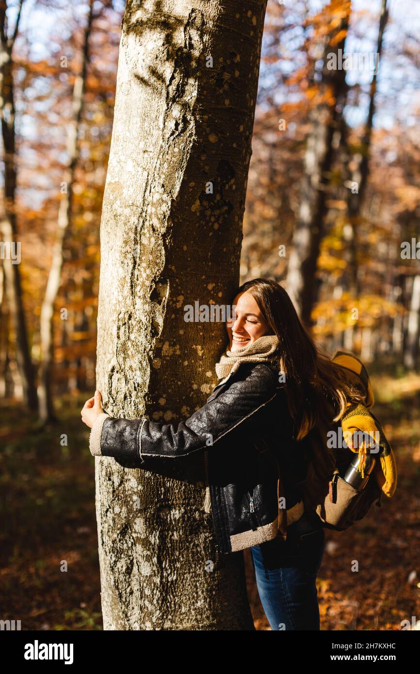 Smiling young woman hugging tree in autumn forest Stock Photo - Alamy