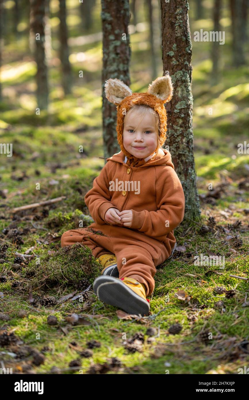 Cute girl sitting in front of tree trunk Stock Photo - Alamy