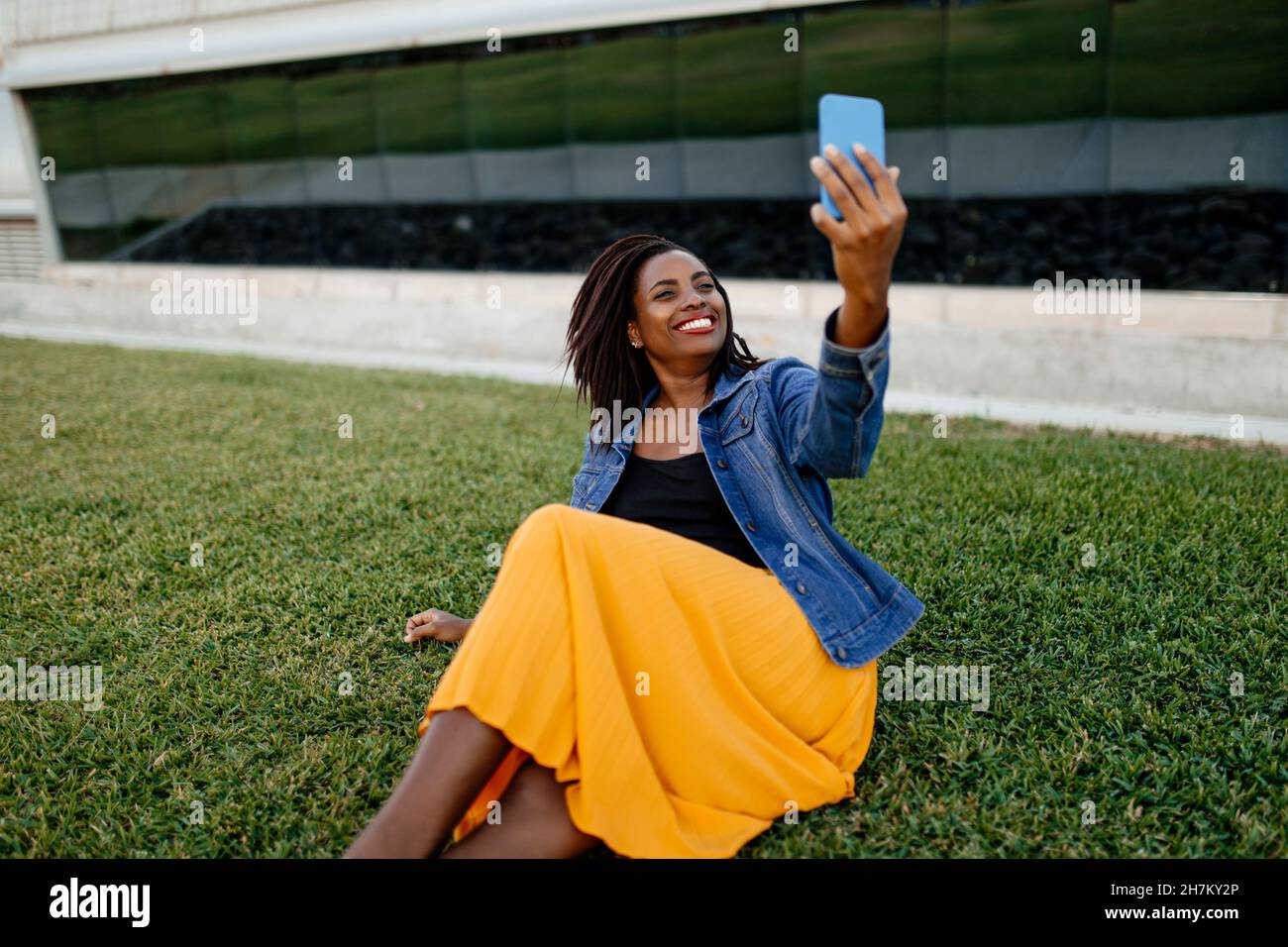 Woman talking selfie through smart phone sitting on grass Stock Photo ...