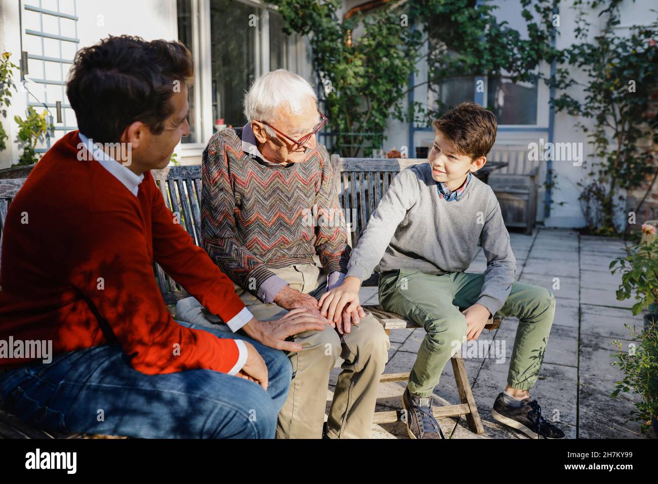 Caring boy and father touching hands of grandfather in backyard Stock ...