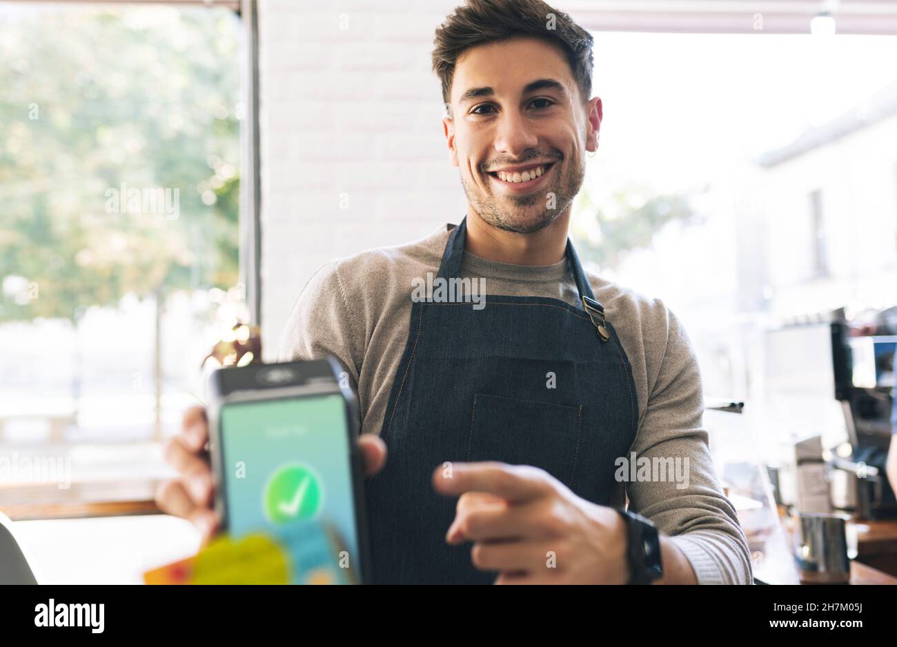 Smiling waiter showing check mark symbol on card reader screen at cafe ...