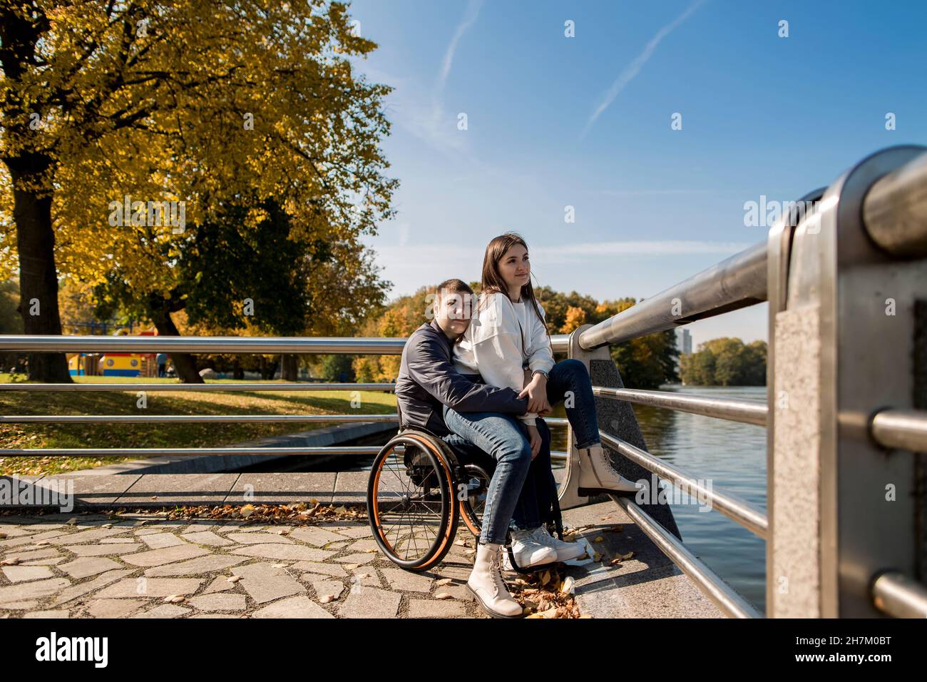 Girlfriend sitting with disabled boyfriend in wheelchair at embankment ...