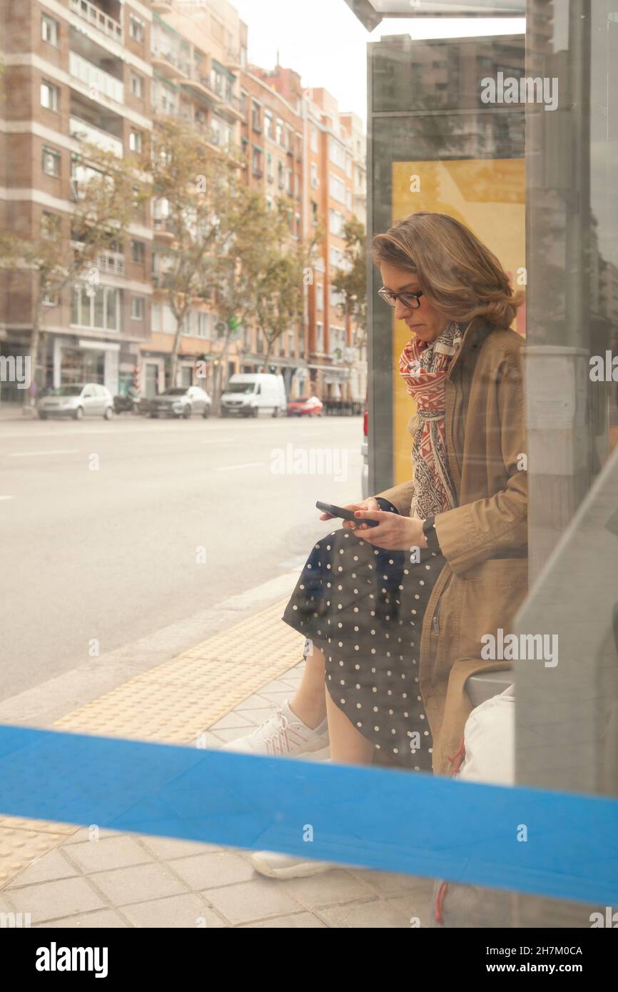 Woman using mobile phone at bus stop Stock Photo - Alamy