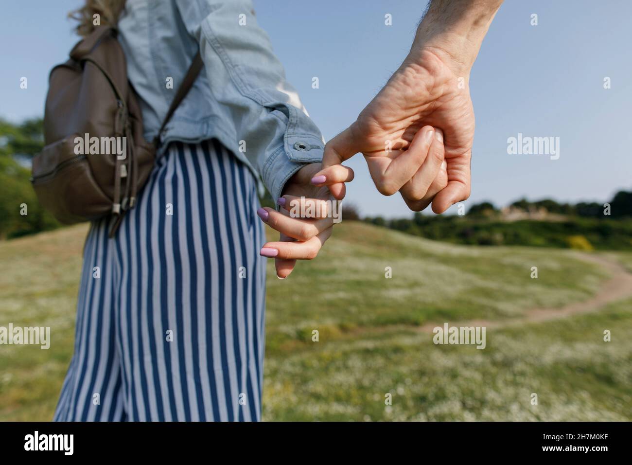 Woman holding pinky finger with boyfriend walking at meadow Stock Photo ...