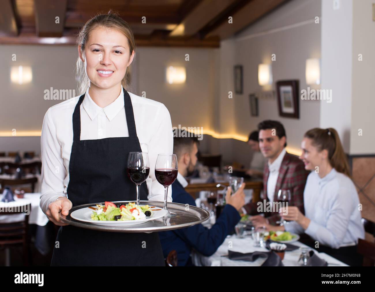 Young positive waitress meeting restaurant guests Stock Photo - Alamy