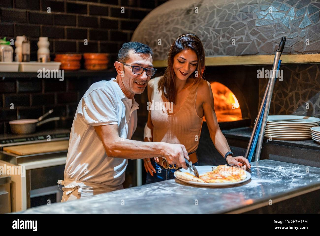 Restaurant manager examining smiling pizza maker working in kitchen ...