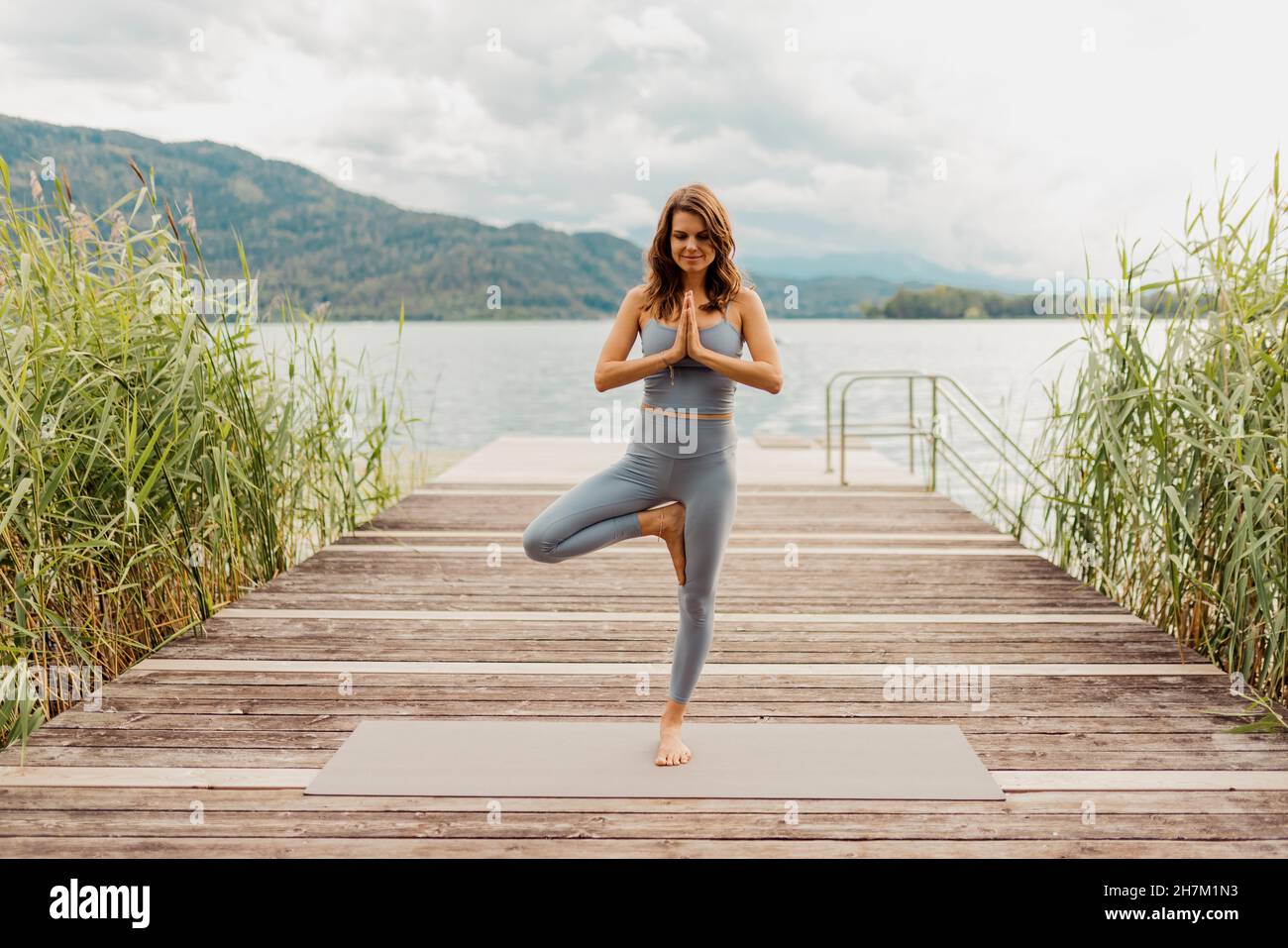 Woman doing tree pose while meditating on jetty Stock Photo - Alamy