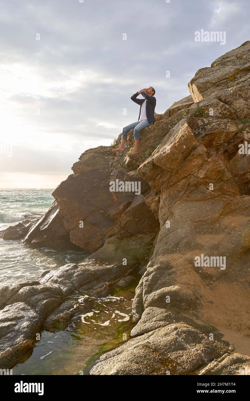 Man sitting on rock shouting at beach Stock Photo - Alamy