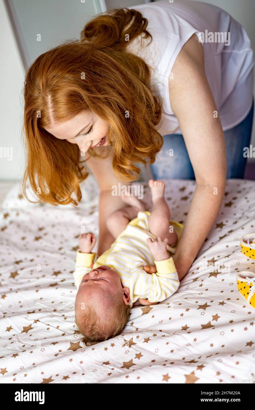 Top view portrait cute newborn redhead baby in childish overalls lying crib during mother ...