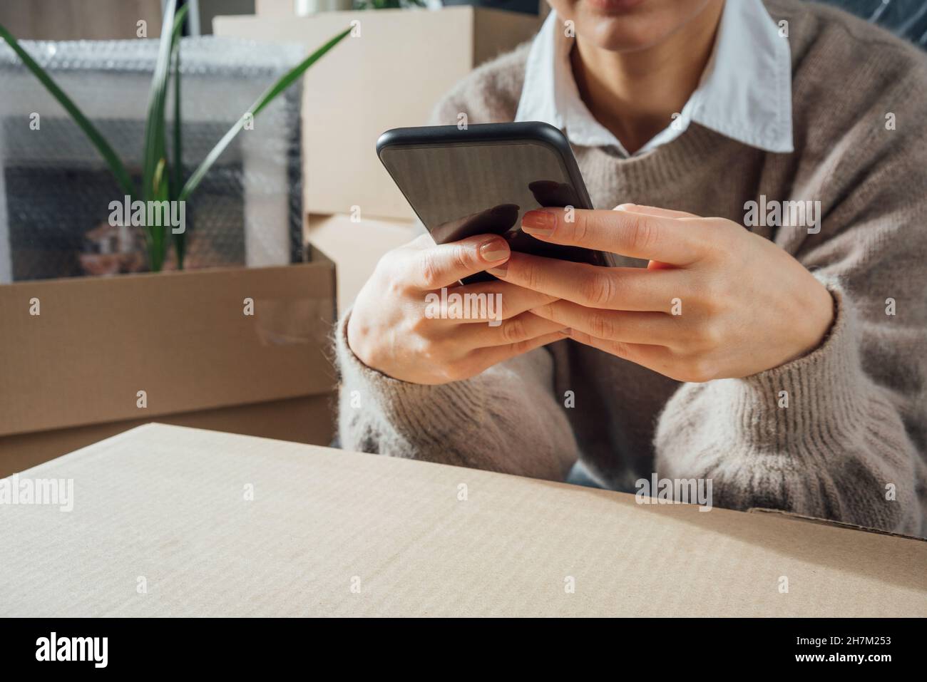 Woman text messaging at cardboard box in new home Stock Photo - Alamy