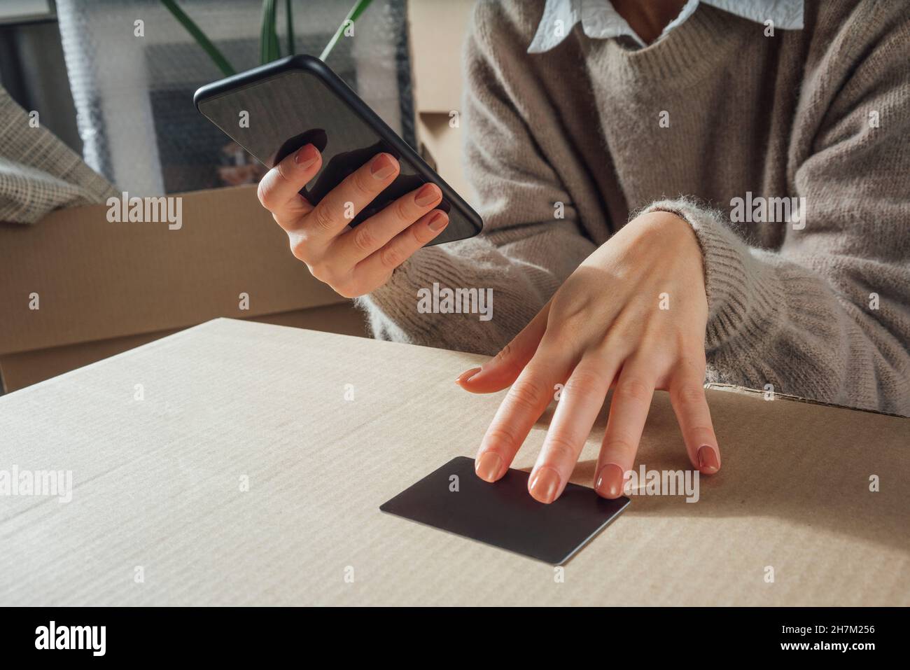 Woman with credit card on carton using mobile phone at home Stock Photo ...