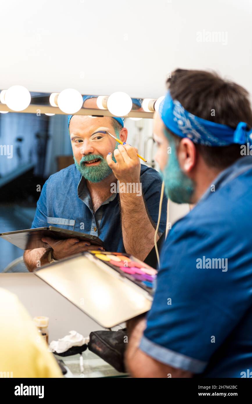 Smiling friends applying drag queen makeup on face at dressing room ...