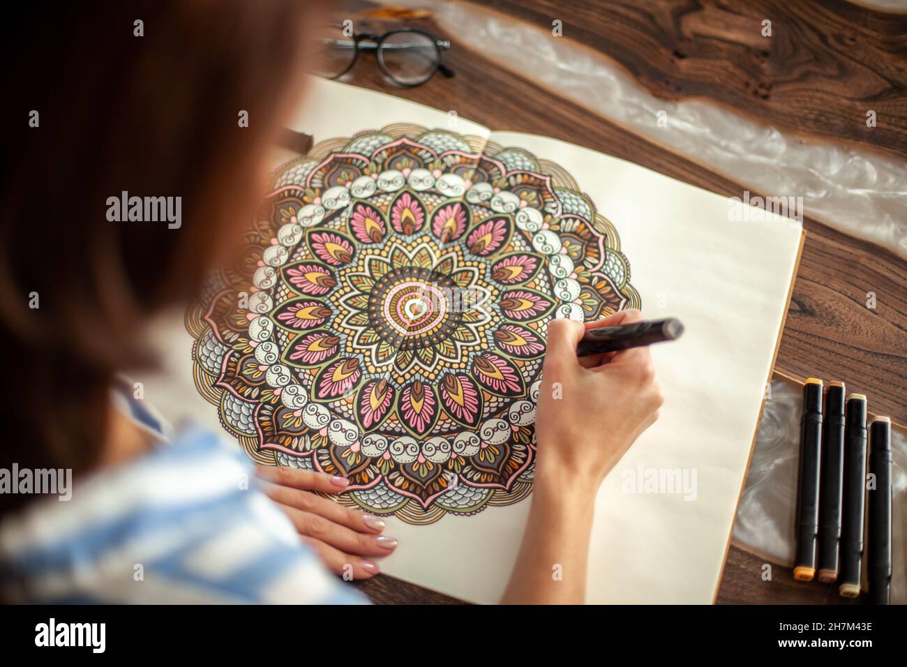 Young beautiful girl with long hair draws a circular mandala pattern ...