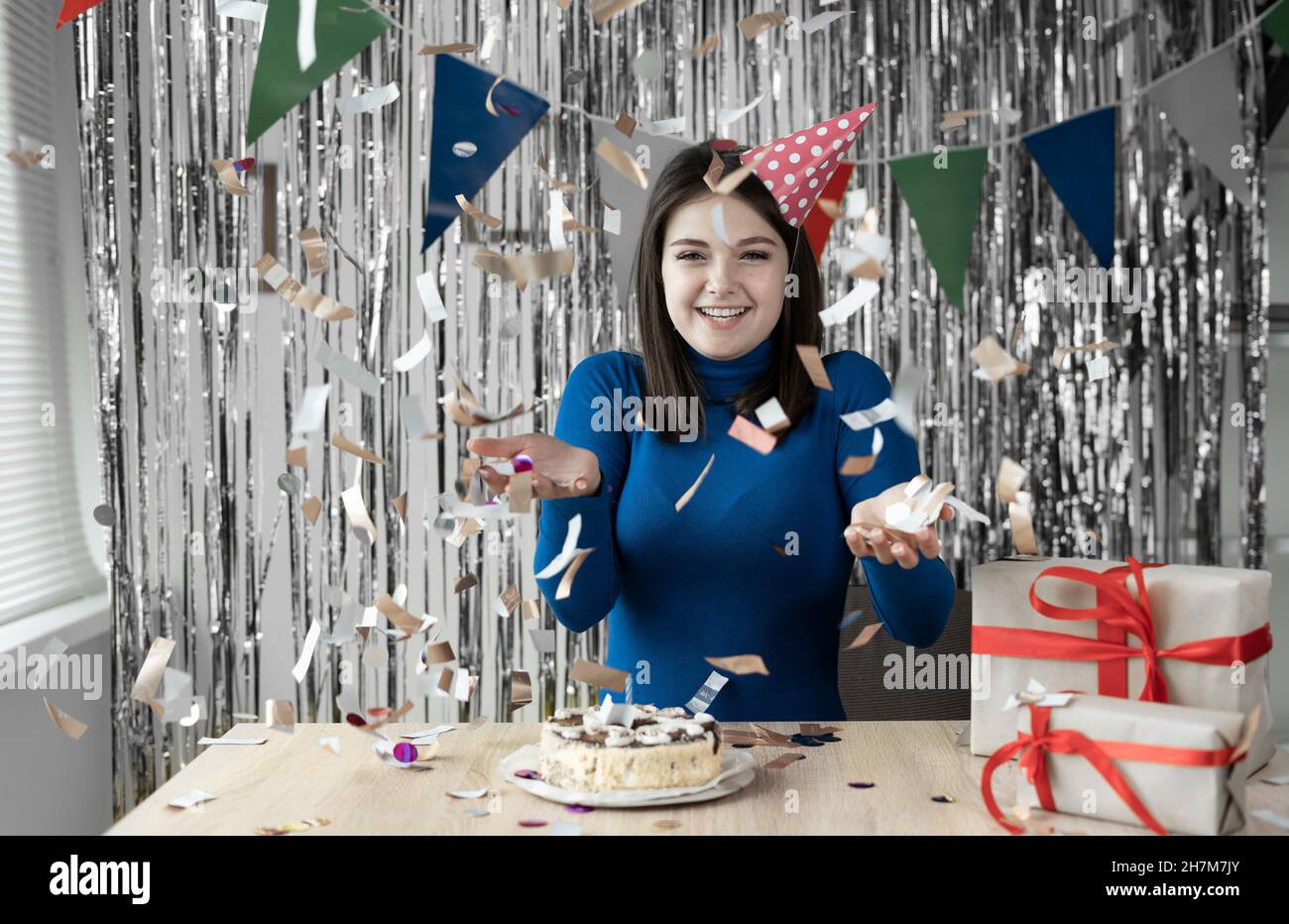 woman in a festive cap sits at the table at home and celebrates her ...