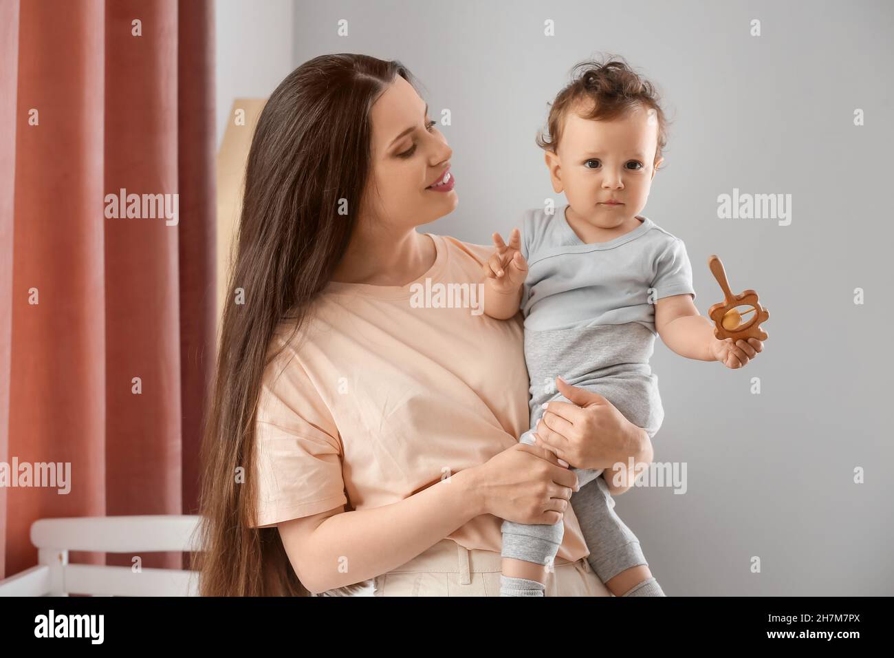 Young mother holding cute little baby with rattle at home Stock Photo - Alamy