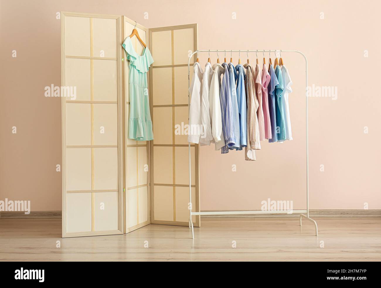 Stylish folding screen and rack with female clothes near wall in room ...