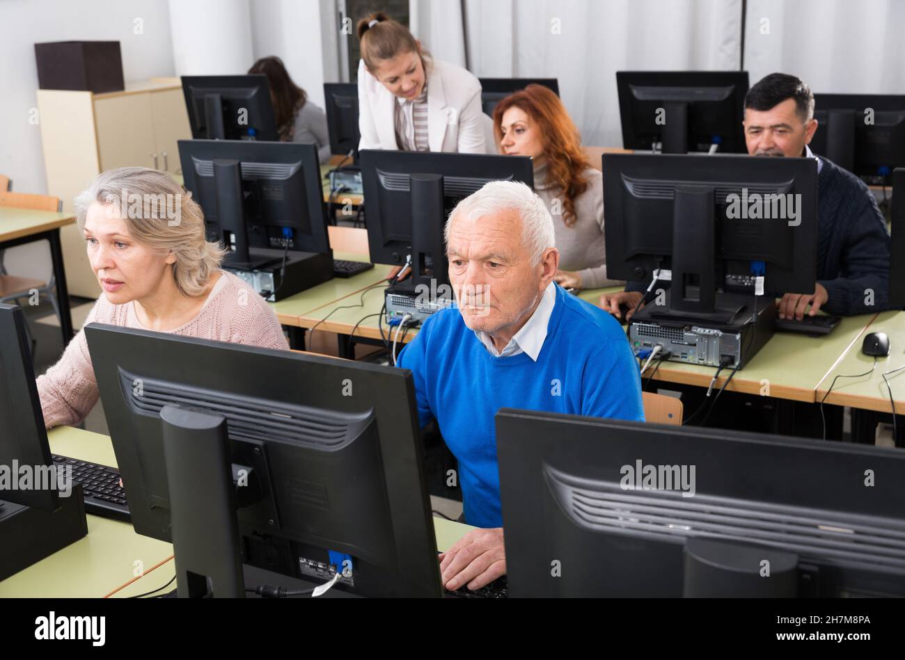 Elderly people working on computers with young teacher Stock Photo - Alamy