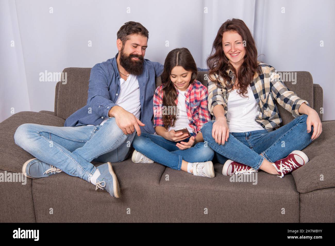 Smartphone obsessed kid. Child use mobile phone sitting next to parents ...