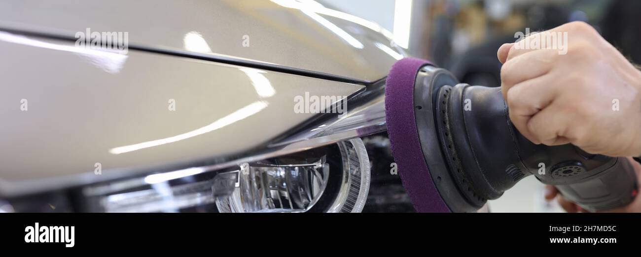 Master repairman polishing headlights of car in workshop using machine ...