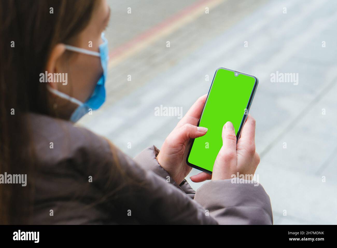 Woman in protective mask holding smart phone with blanck green screen ...
