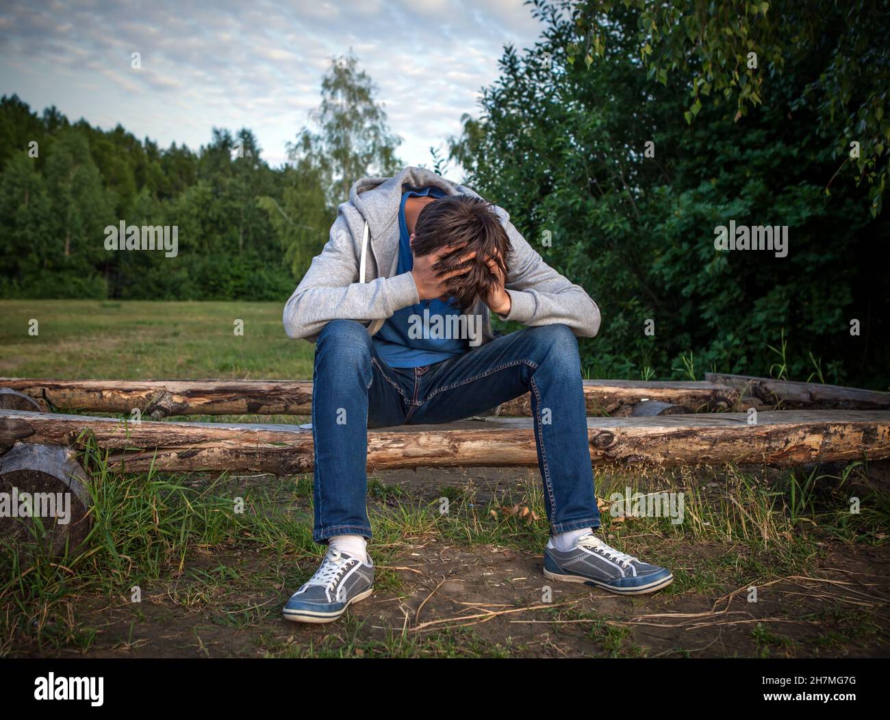 Sad Young Man sit on the Log outdoor Stock Photo - Alamy
