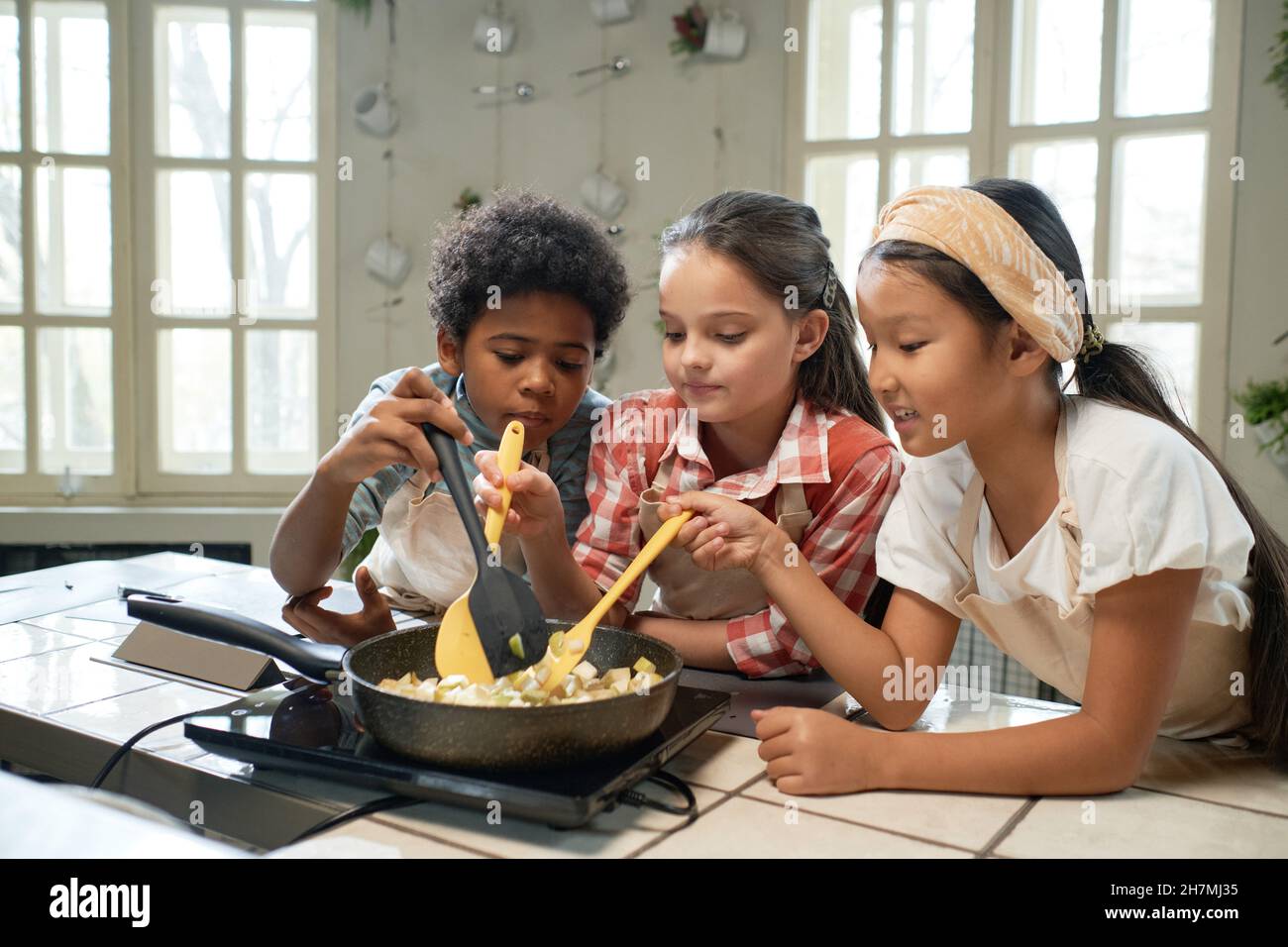 Group of children eating food from the pan at the table during cooking ...