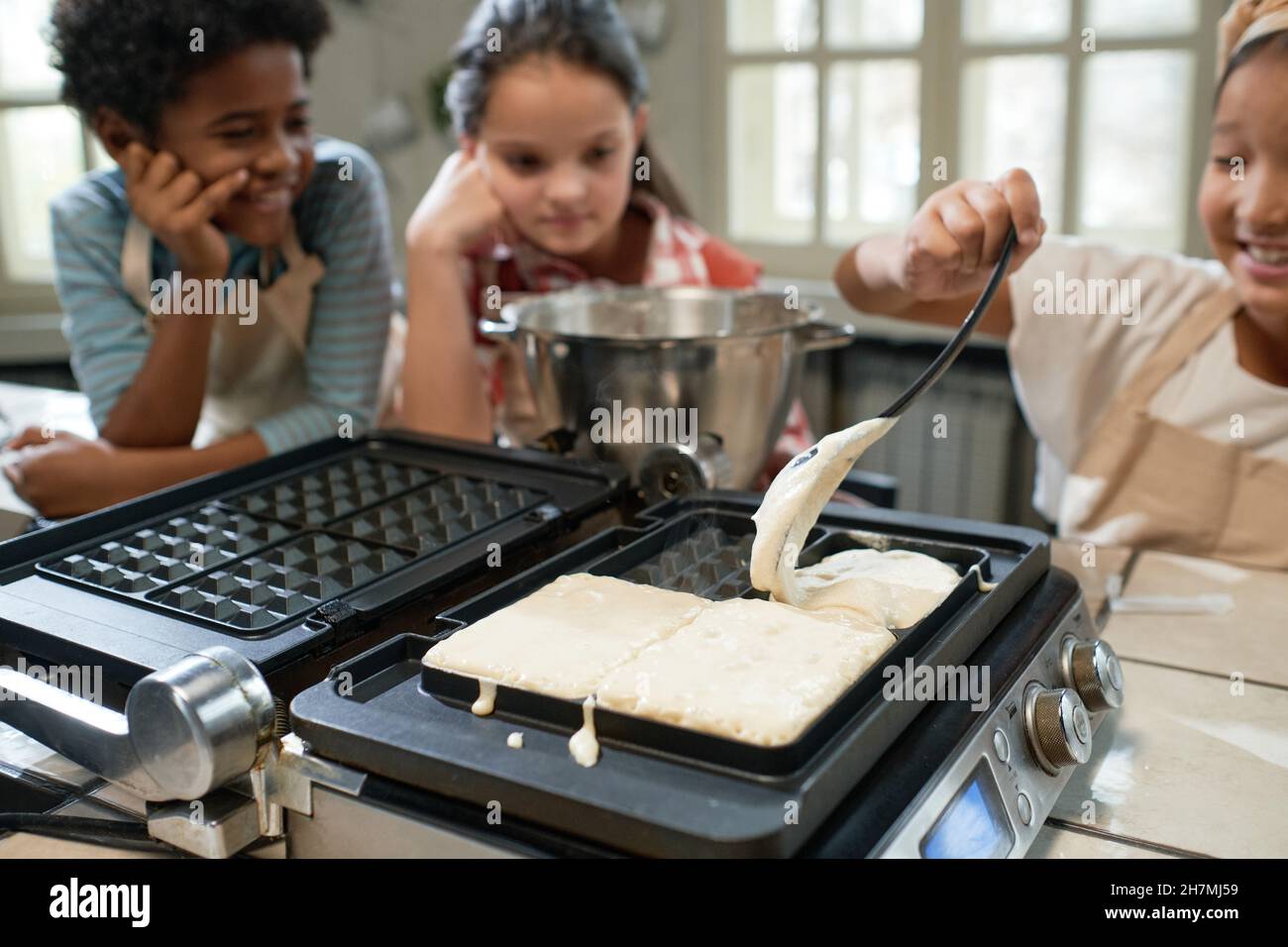 Little girl learning to bake waffles during a lesson with other ...