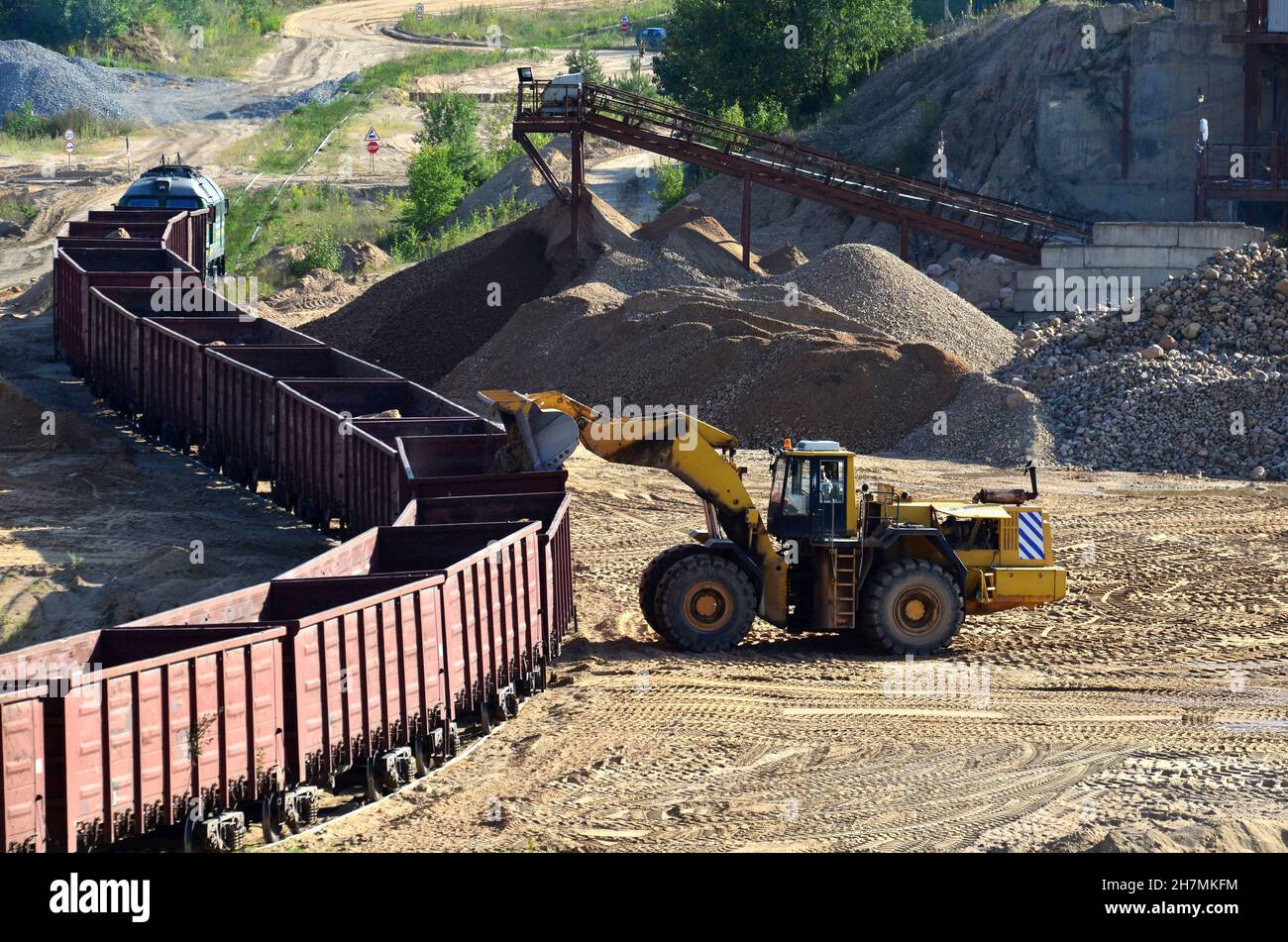 Large heavy front-end loader loading sand it to the freight train ...