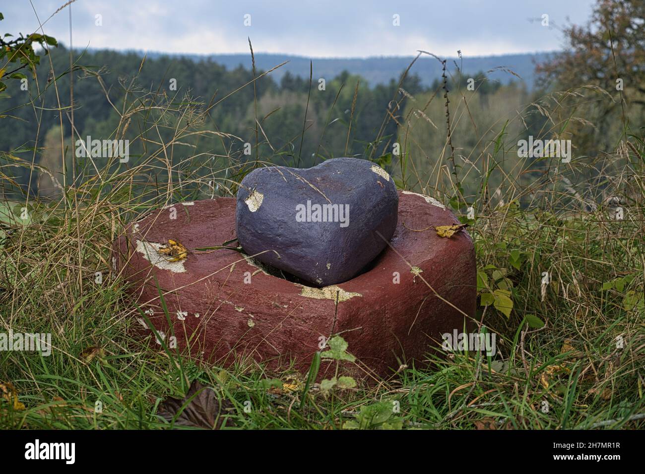 purple stone heart on the roadside in front of a meadow, forest. A sign ...