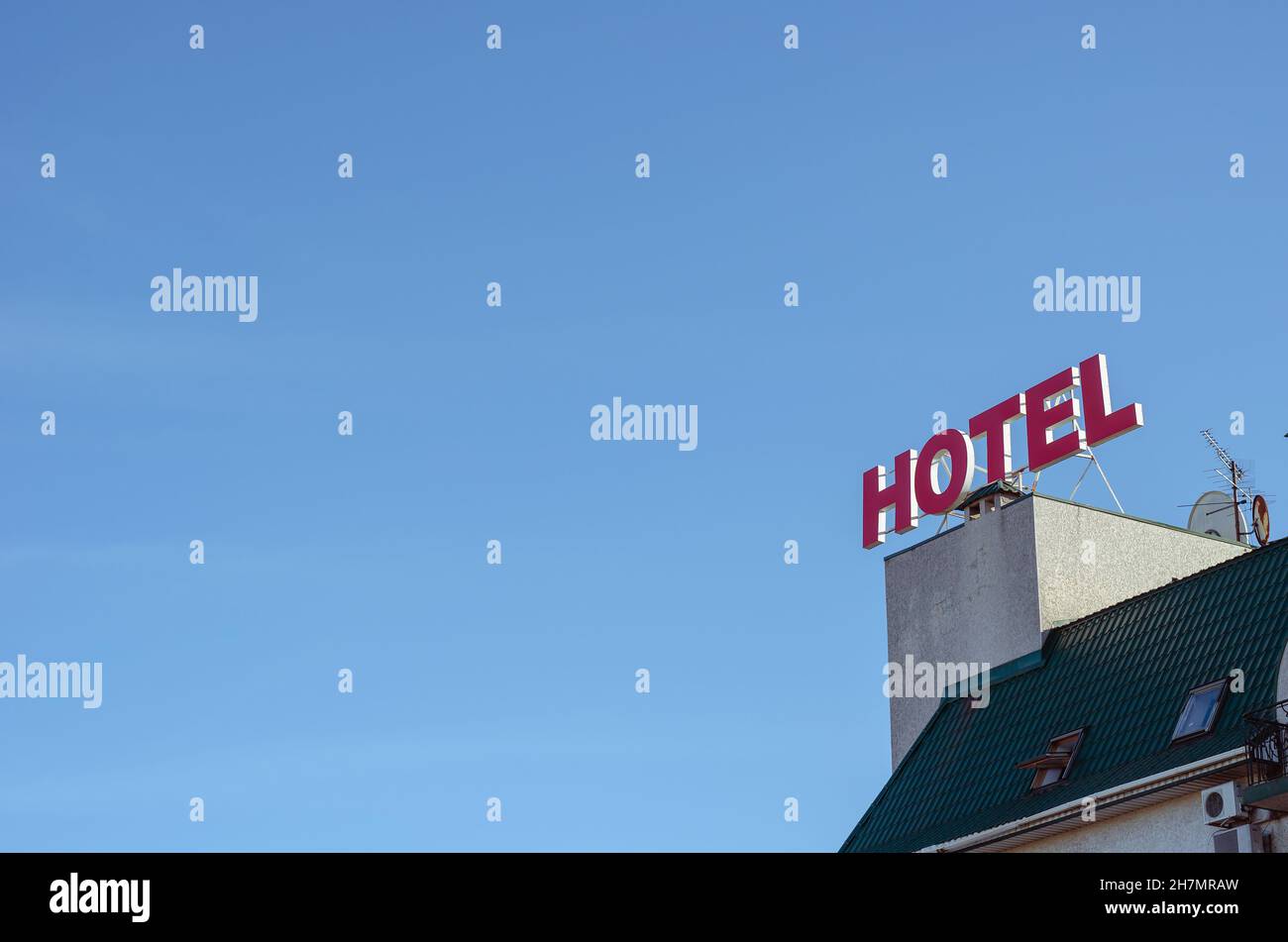 The red neon sign for the HOTEL on the roof of the building. Green roof ...