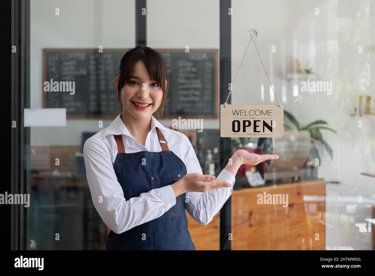 Portrait of a smiling Asian entrepreneur standing behind her cafe ...