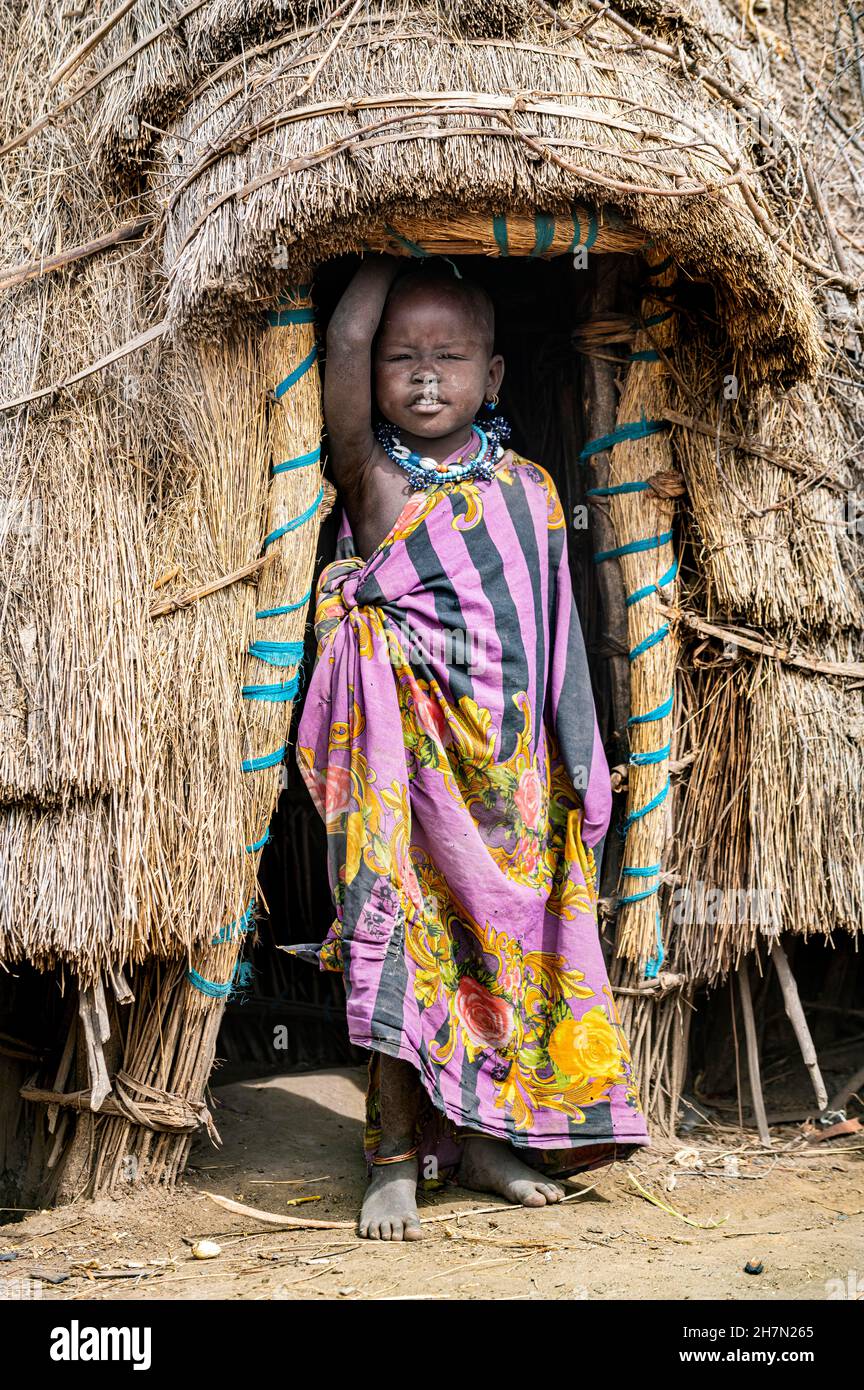 Traditional dressed child of the Jiye tribe standing in her hut ...