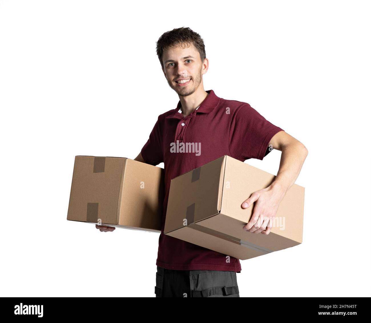 Smiling delivery man holding pile of cardboard boxes on a white ...