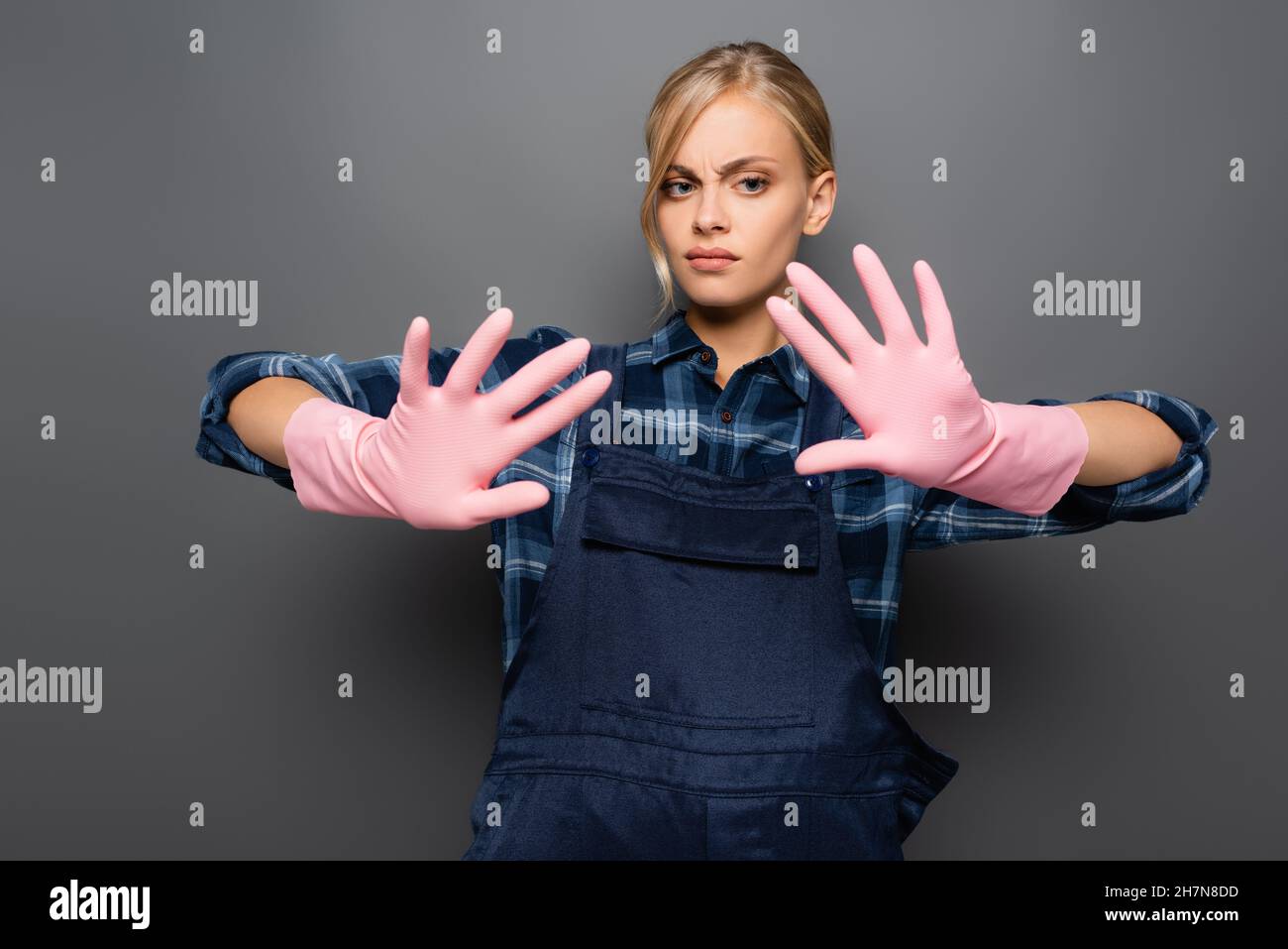 Confused plumber looking at hands in rubber gloves on grey Stock Photo ...