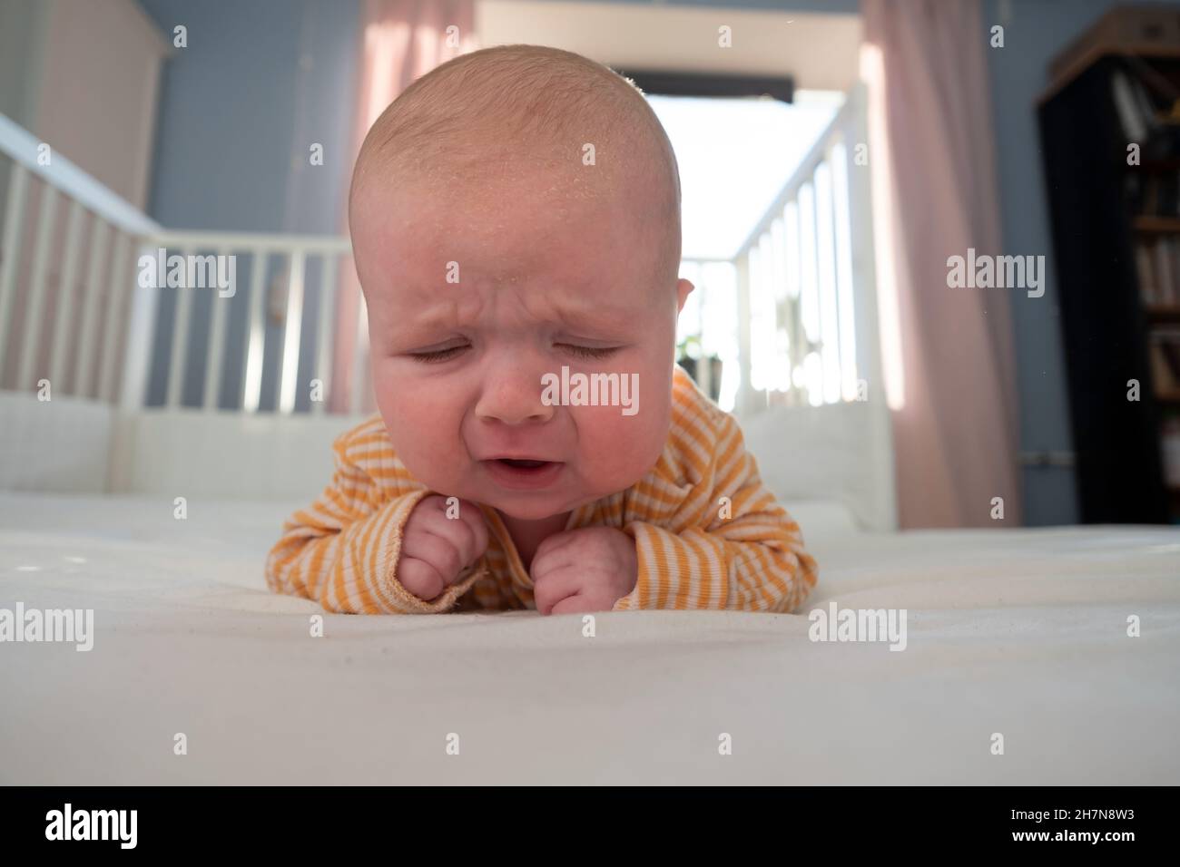 Portrait of crying baby girl lying alone on bed Stock Photo - Alamy