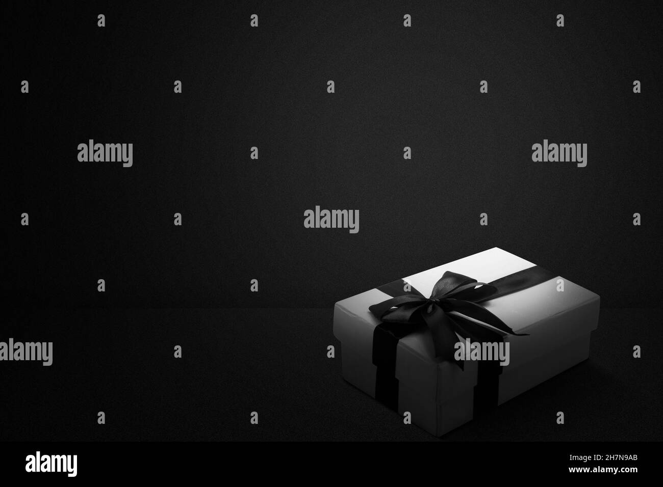 White gift box with a black ribbon with a black background. Black ...