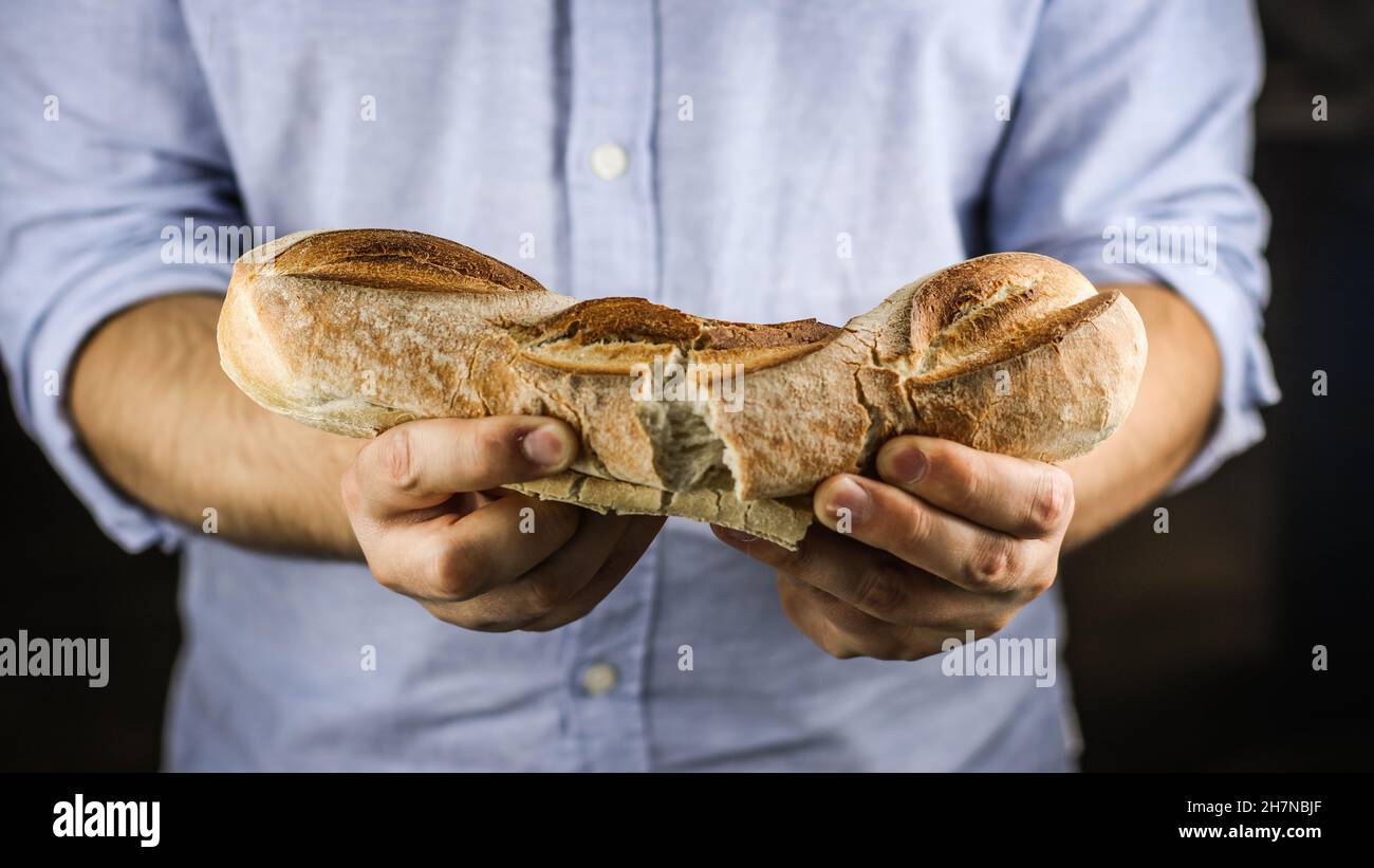 Close-up shot of a man halving the bread into two parts Stock Photo - Alamy