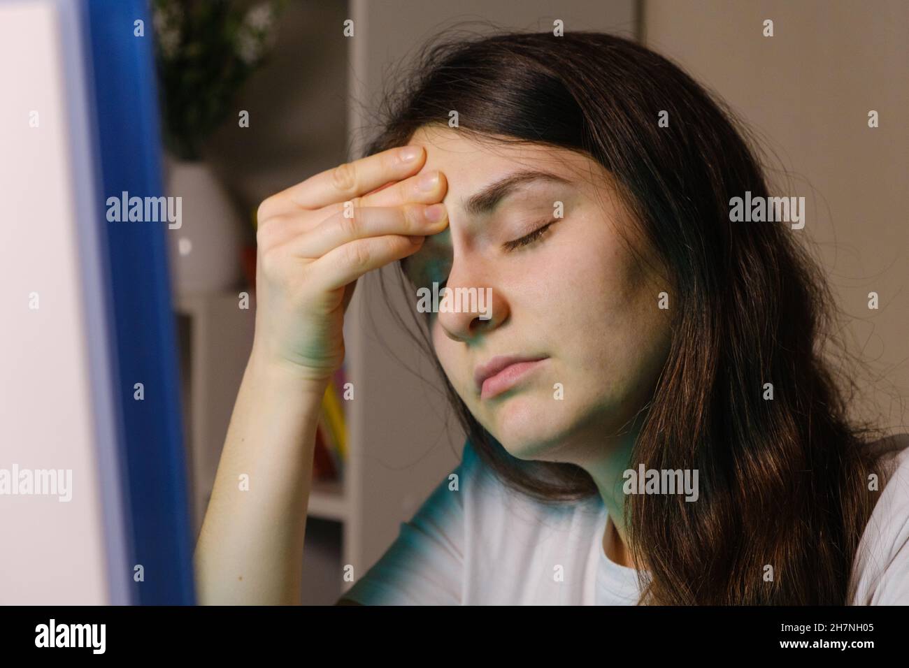 A tired woman holds her hand by the forehead, sitting in front of a ...