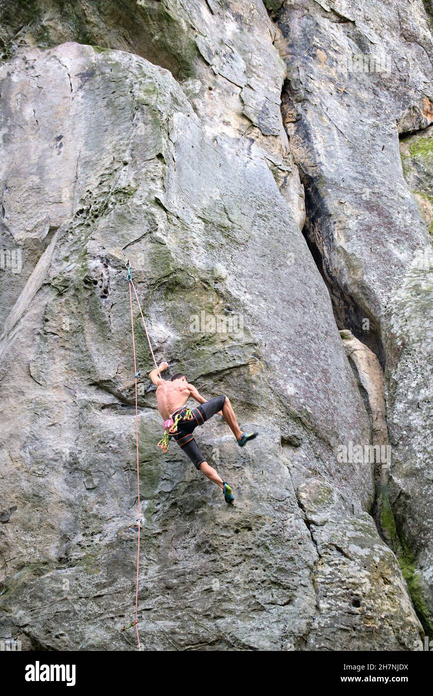 Young man climbing steep wall of rocky mountain. Male climber overcomes ...