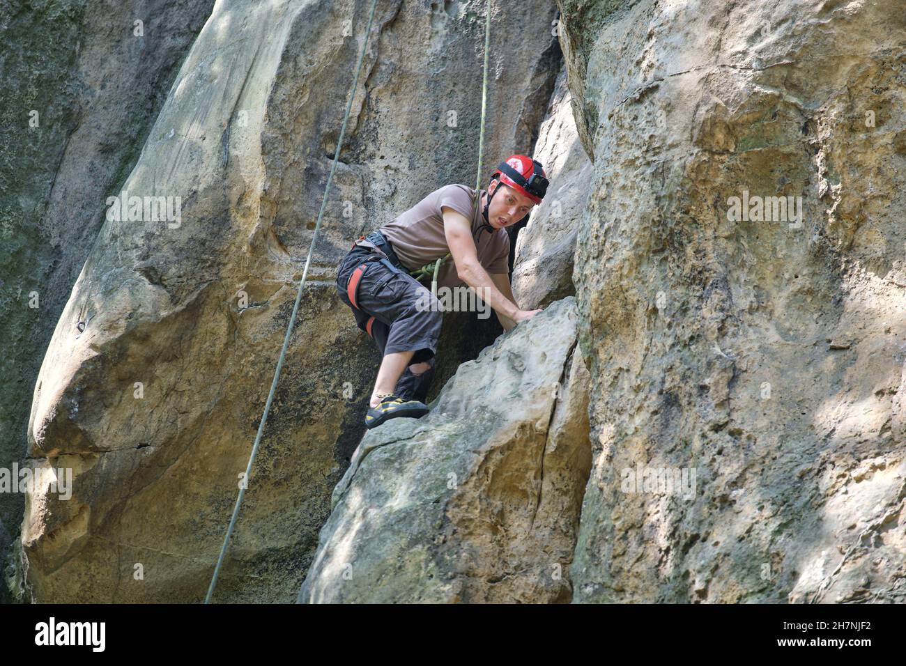 Young man climbing steep wall of rocky mountain. Male climber overcomes ...