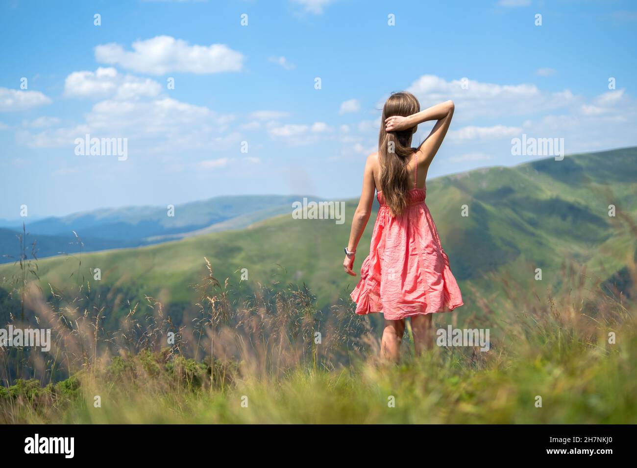 Young happy woman in red dress walking on grass field on a windy day in ...
