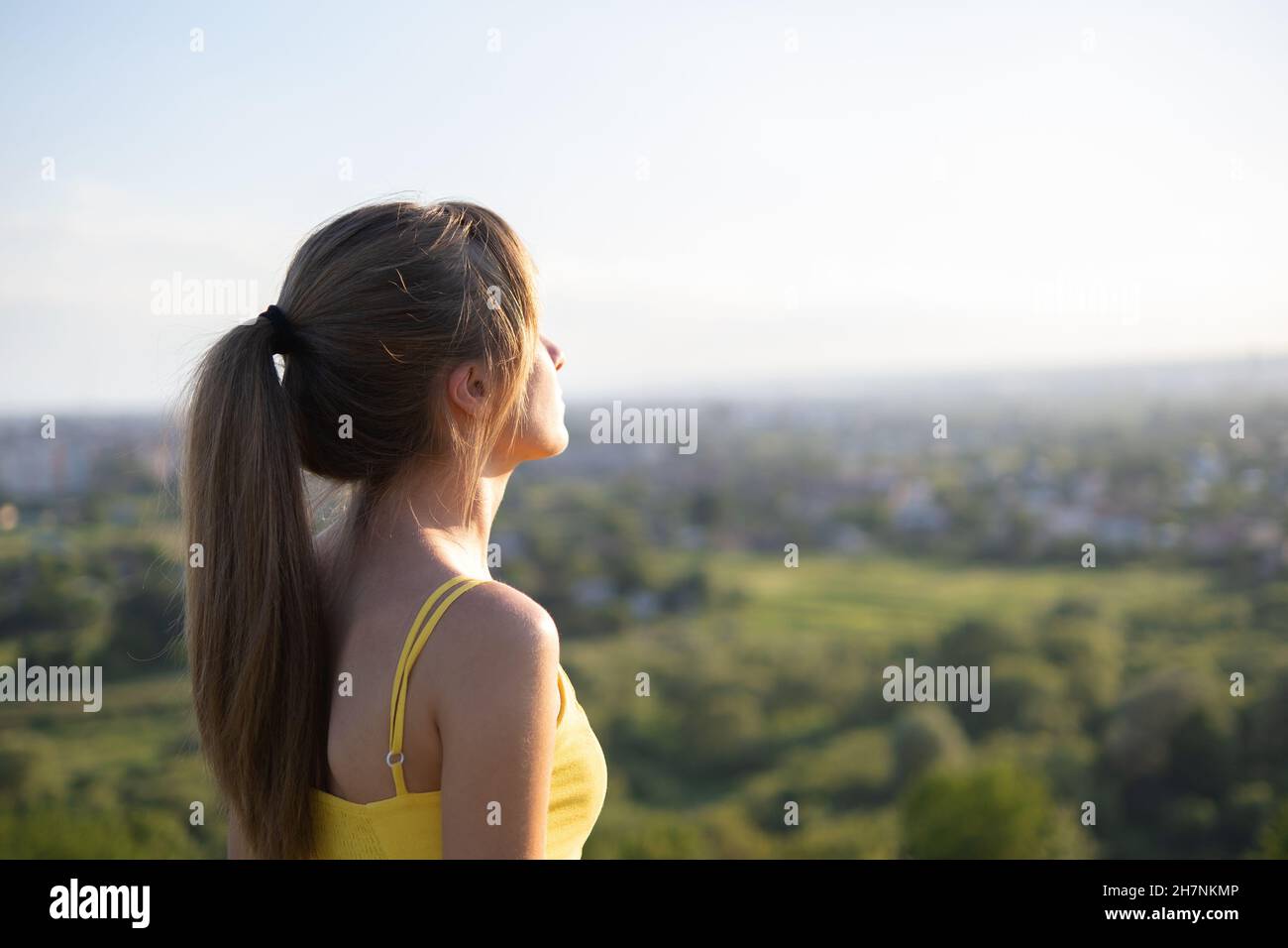 Young relaxed woman standing in green field looking at sunset view in ...
